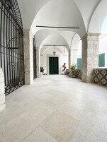 Um corredor espaçoso com teto alto, uma porta verde no final e um papel de parede estampado à direita.
