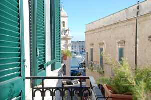Uma rua estreita ladeada por edifícios, uma igreja com um campanário e vista para barcos na água.