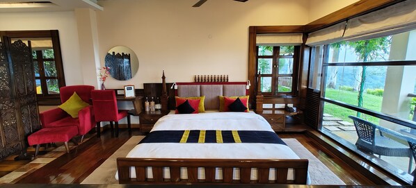 Um quarto espaçoso com uma cama grande, uma poltrona vermelha e vista para o exterior através de amplas janelas.