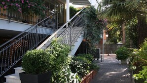 Uma escadaria com guarda-corpos de metal, rodeada por vegetação exuberante e plantas em vasos.