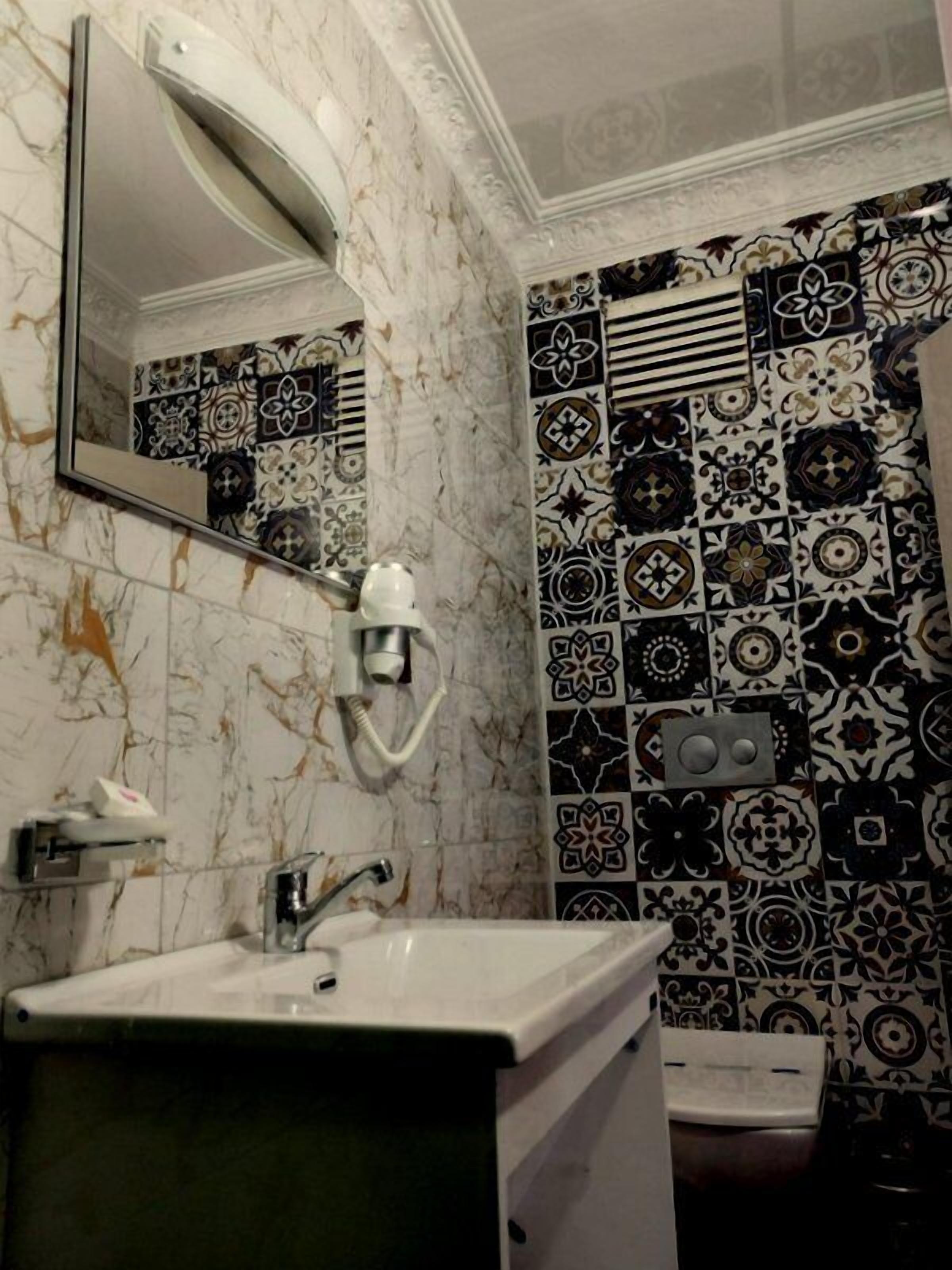 Um banheiro com parede de mármore, pia com espelho e ladrilhos estampados.