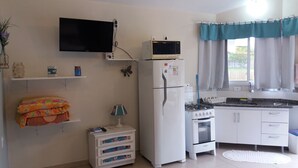 Uma cozinha compacta com geladeira, micro-ondas, fogão e uma TV de tela plana.