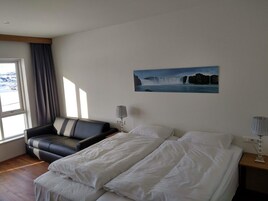 Quarto de hotel com cama, sofá, quadro de uma cascata e janela com cortinas.