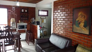 Um espaço compacto com cozinha, mesa de jantar e cadeiras, sofá de couro e uma grande pintura religiosa na parede.