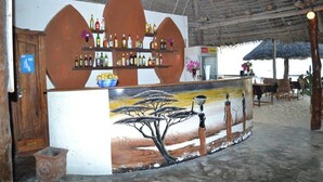 Uma área de bar com um mural de uma árvore e figuras, prateleiras com garrafas e teto rústico.