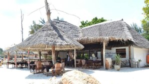 Um restaurante à beira-mar com telhados de palha e mesas ao ar livre.