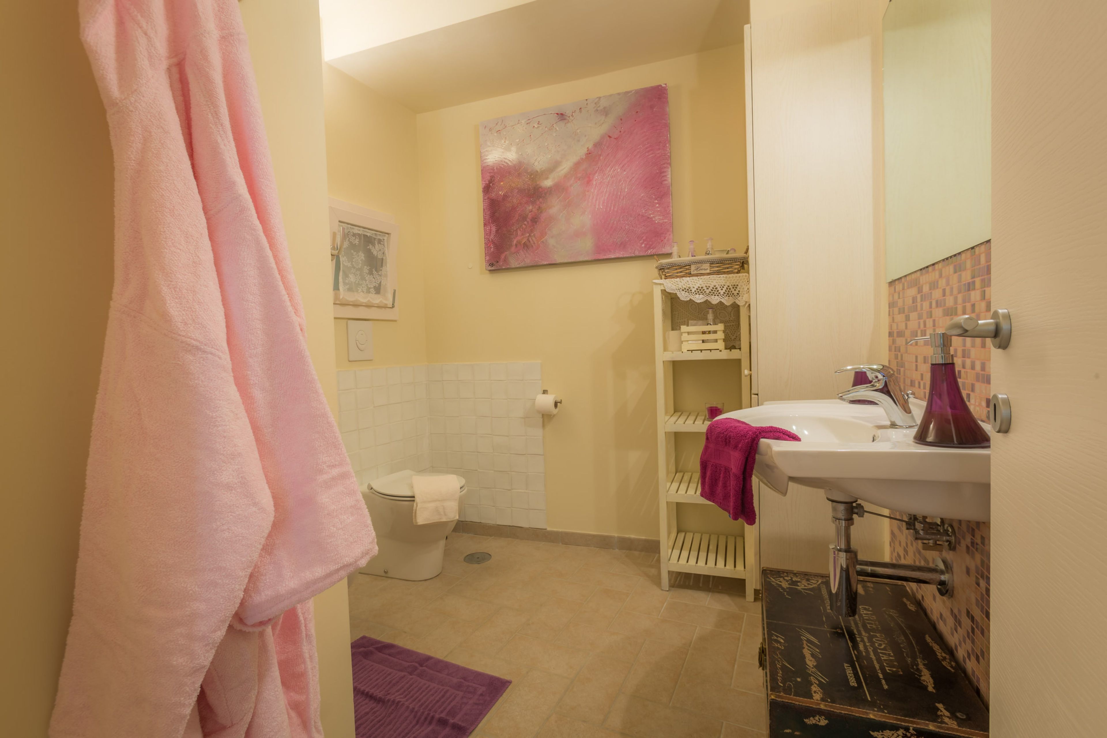 Casa de banho com sanita, lavatório e uma toalha cor-de-rosa pendurada na parede.