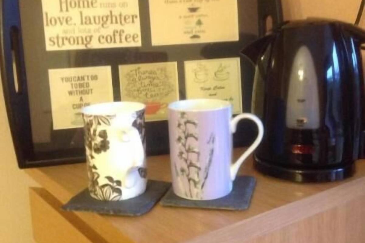 Uma moldura com uma frase numa parede, duas chávenas de café sobre protectores e uma cafeteira numa superfície de madeira.