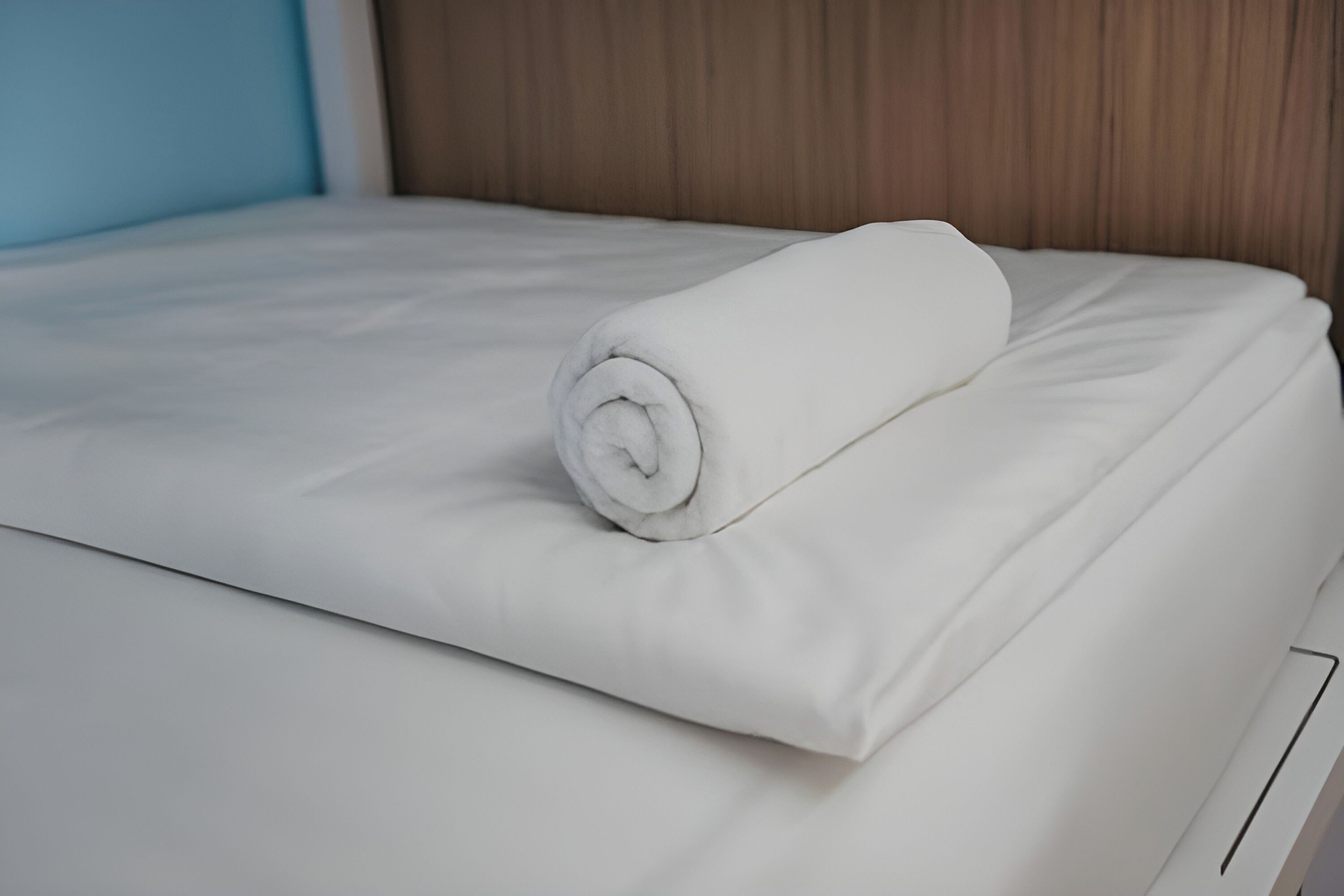 Cama bem arrumada com edredom branco e manta branca enrolada em cabeceira de madeira.