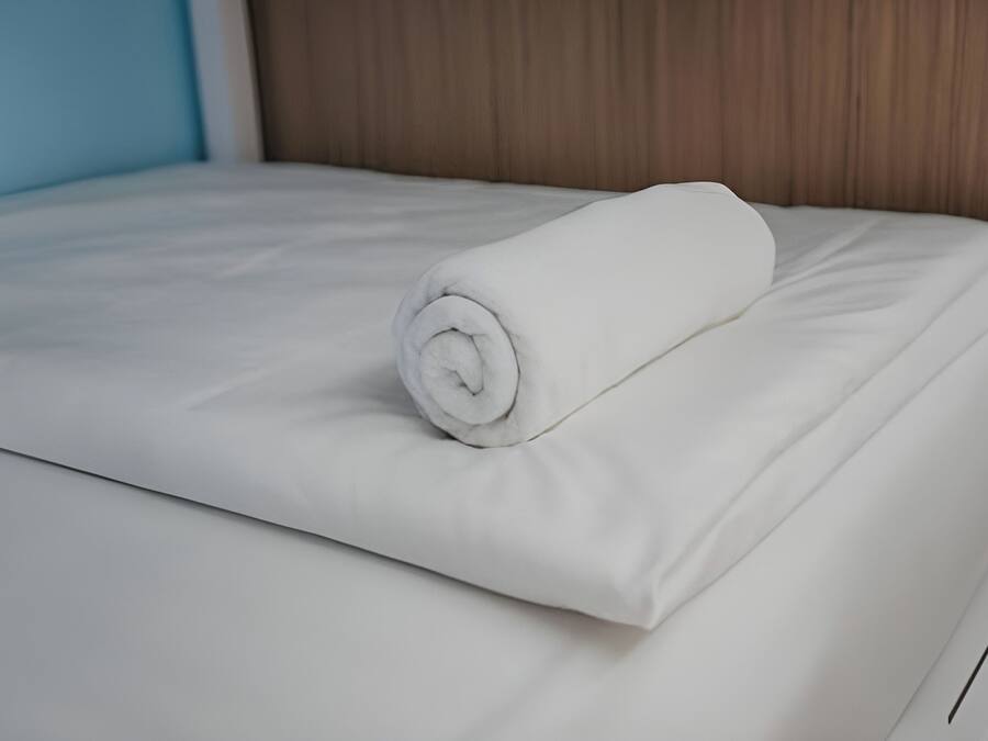 Cama bem arrumada com edredom branco e manta branca enrolada em cabeceira de madeira.