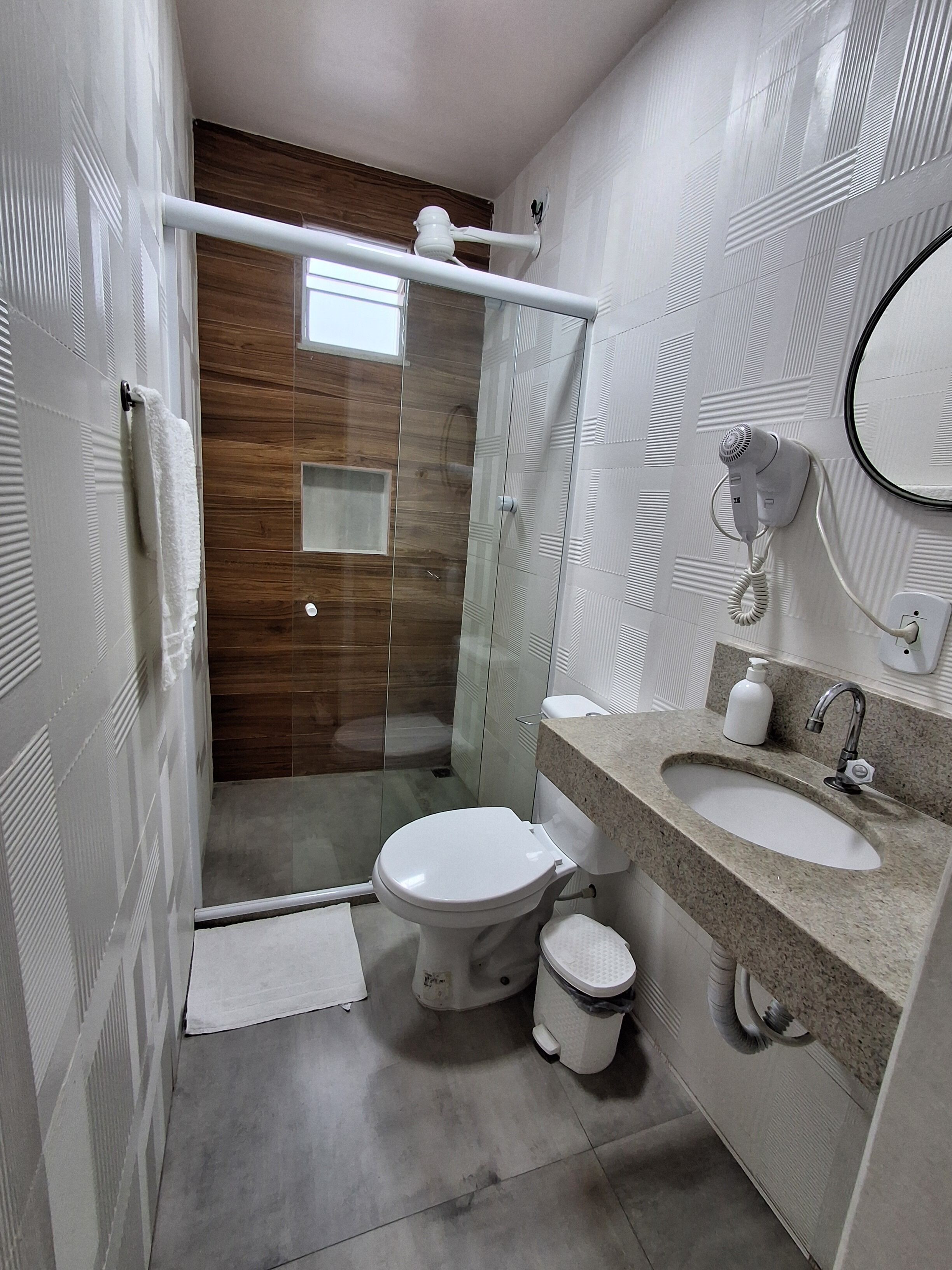 Uma casa de banho moderna com cabine de duche em vidro, sanita, lavatório e espelho.