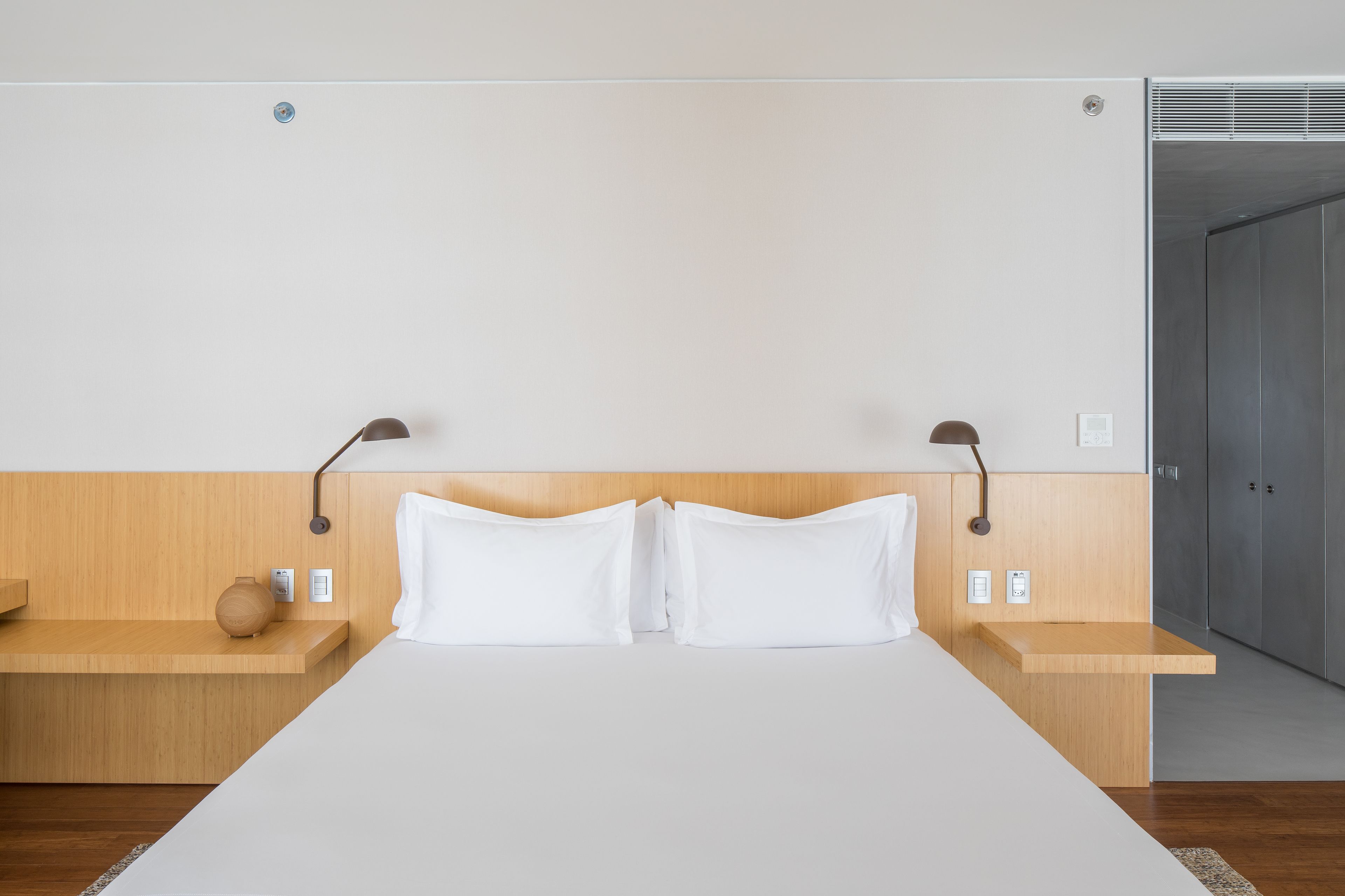 Quarto de hotel moderno com uma cama grande, cabeceira de madeira, mesas de cabeceira e um guarda-roupa embutido.