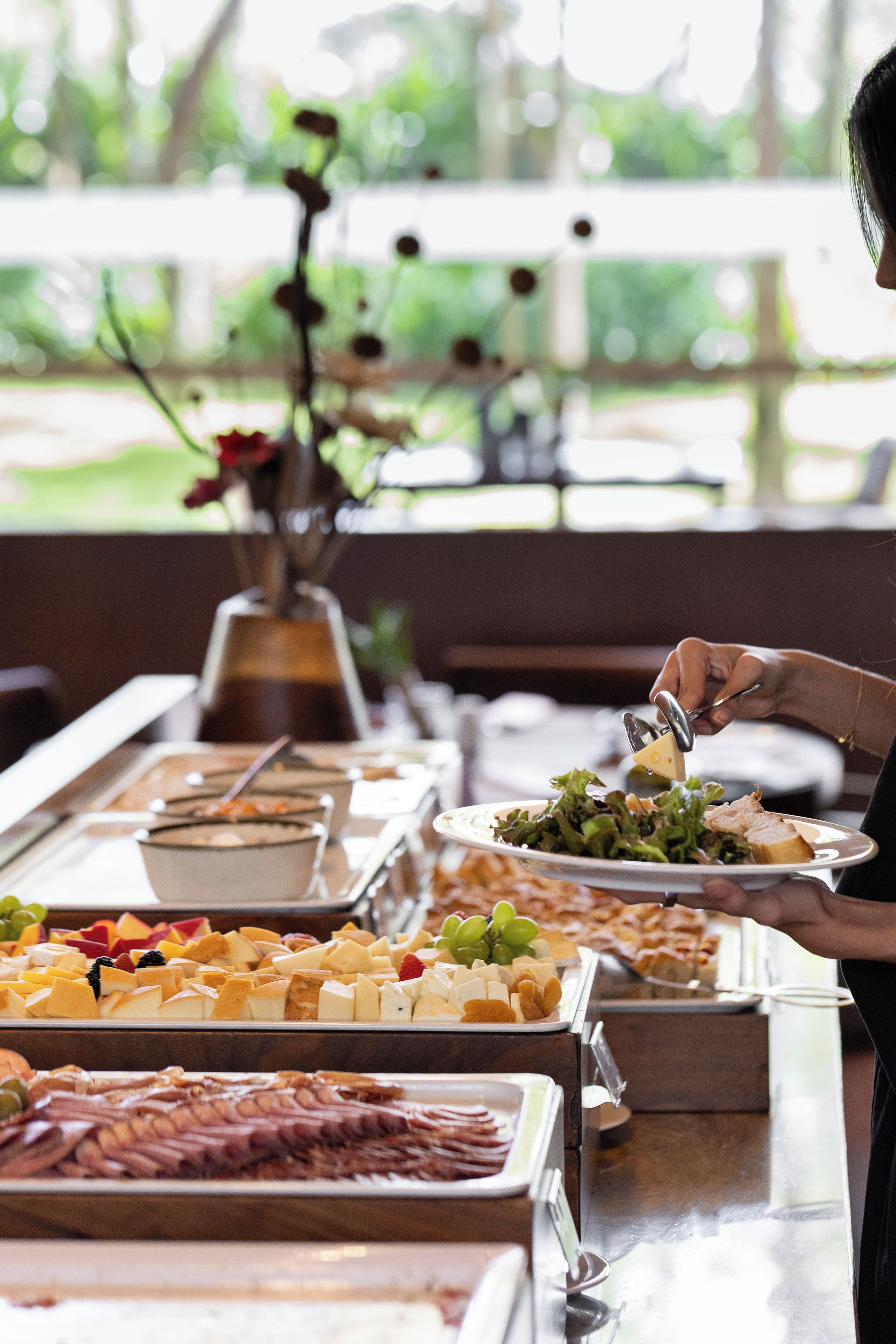 Uma mesa de buffet com diversos alimentos e uma pessoa se servindo.