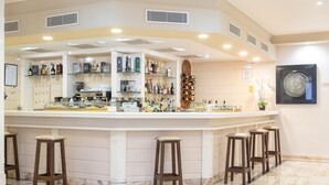 Uma área de bar com piso de mármore, banquetas de madeira e prateleiras repletas de garrafas e copos.