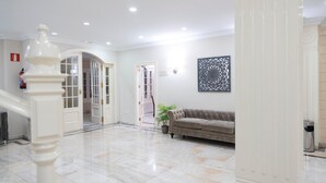 Um hall amplo com piso de mármore, sofá bege e um painel decorativo na parede.
