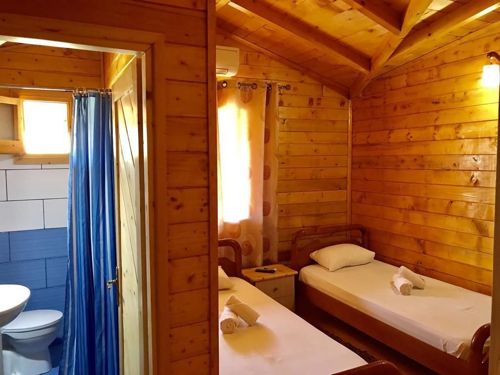 Quarto de cabana de madeira com uma cama de solteiro, uma mesinha e banheiro com cortina de chuveiro.