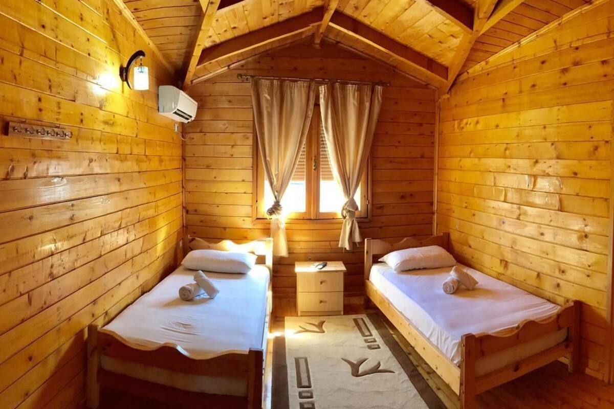 Uma cabana com duas camas de madeira, uma pequena mesa de cabeceira e uma janela com cortinas.