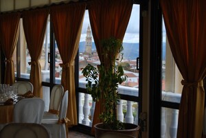 Uma sala de jantar com uma mesa posta para dois, uma planta em vaso e vista de uma torre através de grandes janelas.