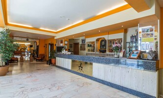 Um hall de hotel com balcão de recepção, área de estar e uma grande planta em vaso.