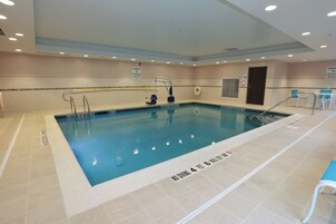 Piscina interior com água cristalina, marcações de profundidade e cadeira do salva-vidas.