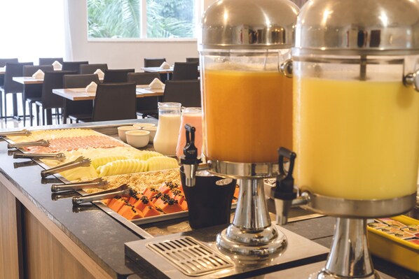 Uma área de buffet com diversos alimentos e um dispensador de sucos.