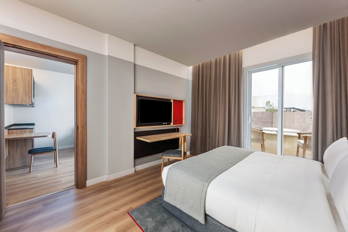 Quarto de hotel moderno com uma cama grande, uma escrivaninha com televisão e uma varanda com vista.