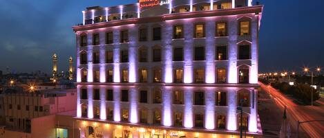 Um hotel de vários andares com letreiros iluminados, entrada destacada e vista para a rua.