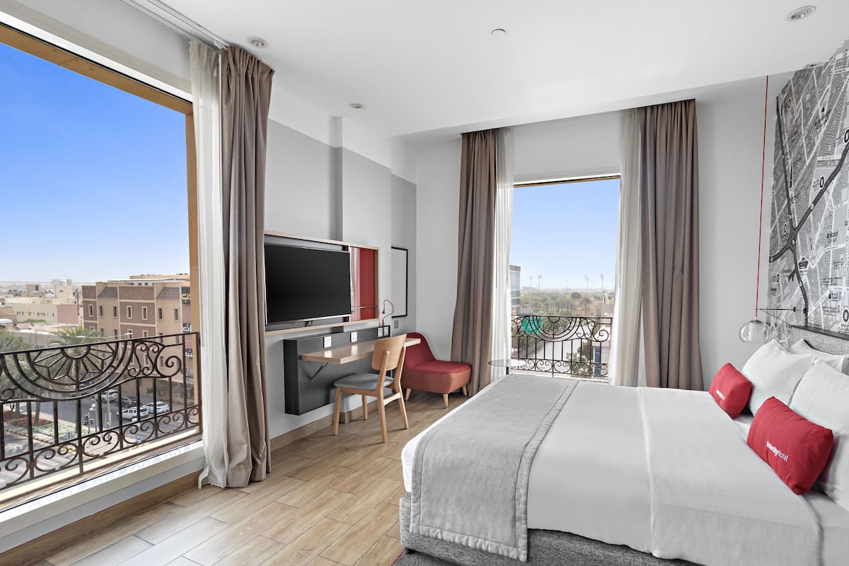 Quarto de hotel moderno com uma cama grande, uma escrivaninha com televisão e uma varanda com vista para a cidade.