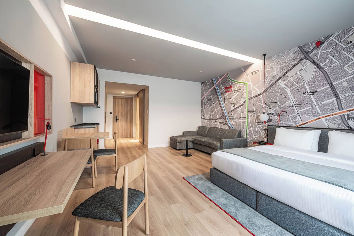 Quarto de hotel moderno com cama, área de estar, mesa de jantar e um mapa na parede.