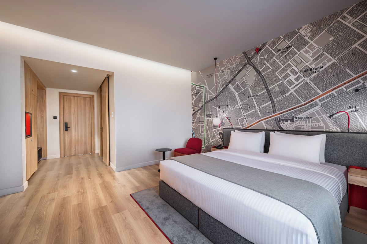 Um quarto com uma cama grande, um mural de mapa, uma cadeira vermelha e uma mesinha.