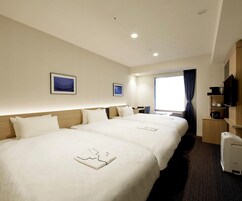 Quarto de hotel com duas camas, uma escrivaninha, uma cadeira, televisão e janela com cortinas.