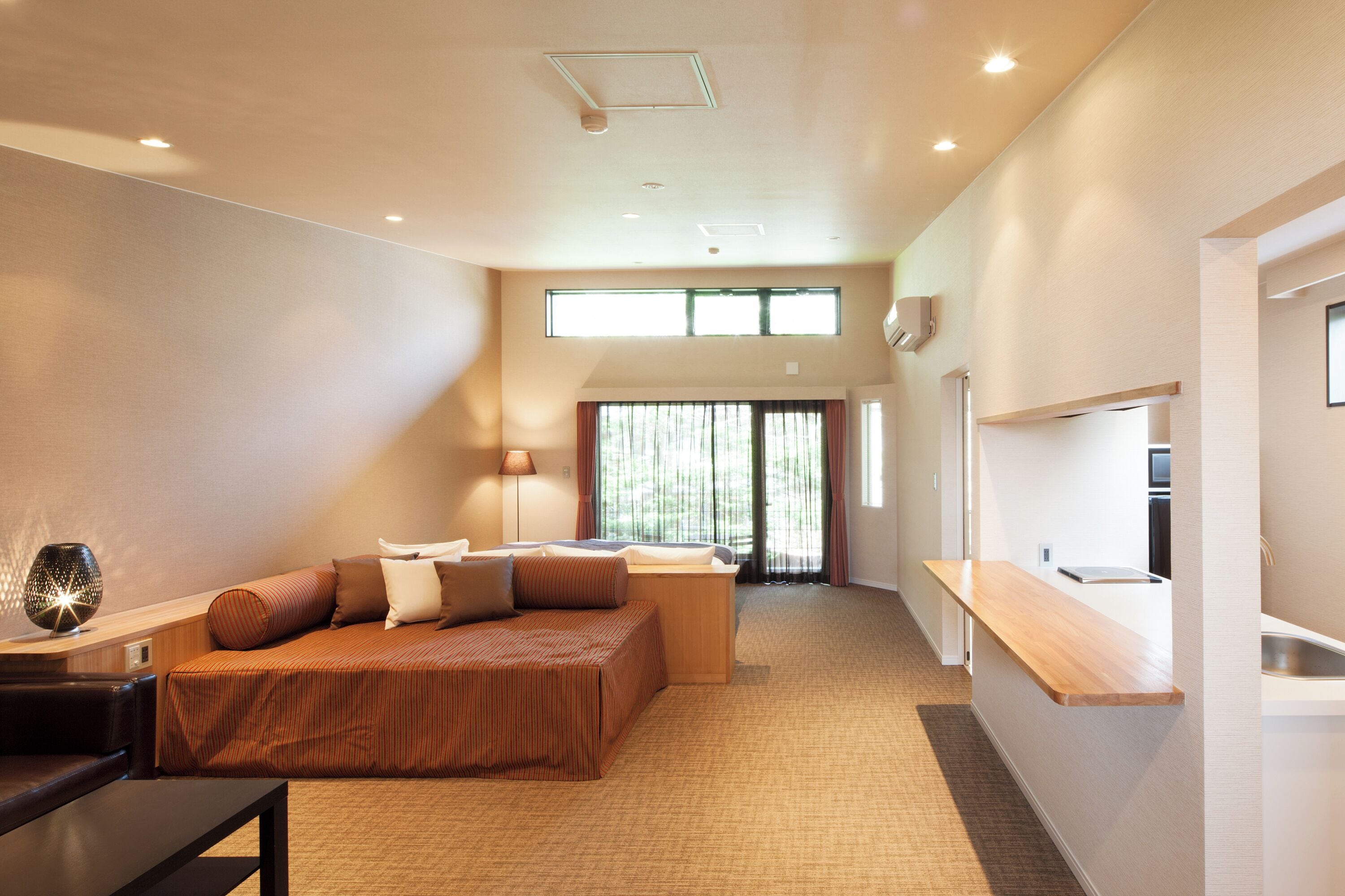 Quarto de hotel moderno com sofá-cama, uma pequena escrivaninha e uma área de kitchenette.