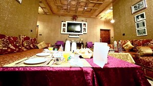 Uma sala de jantar com uma mesa posta para dois, uma televisão na parede e um sofá estampado.