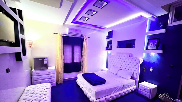 Quarto moderno com uma cama grande, mesas de cabeceira, guarda-roupa e luminária no teto.