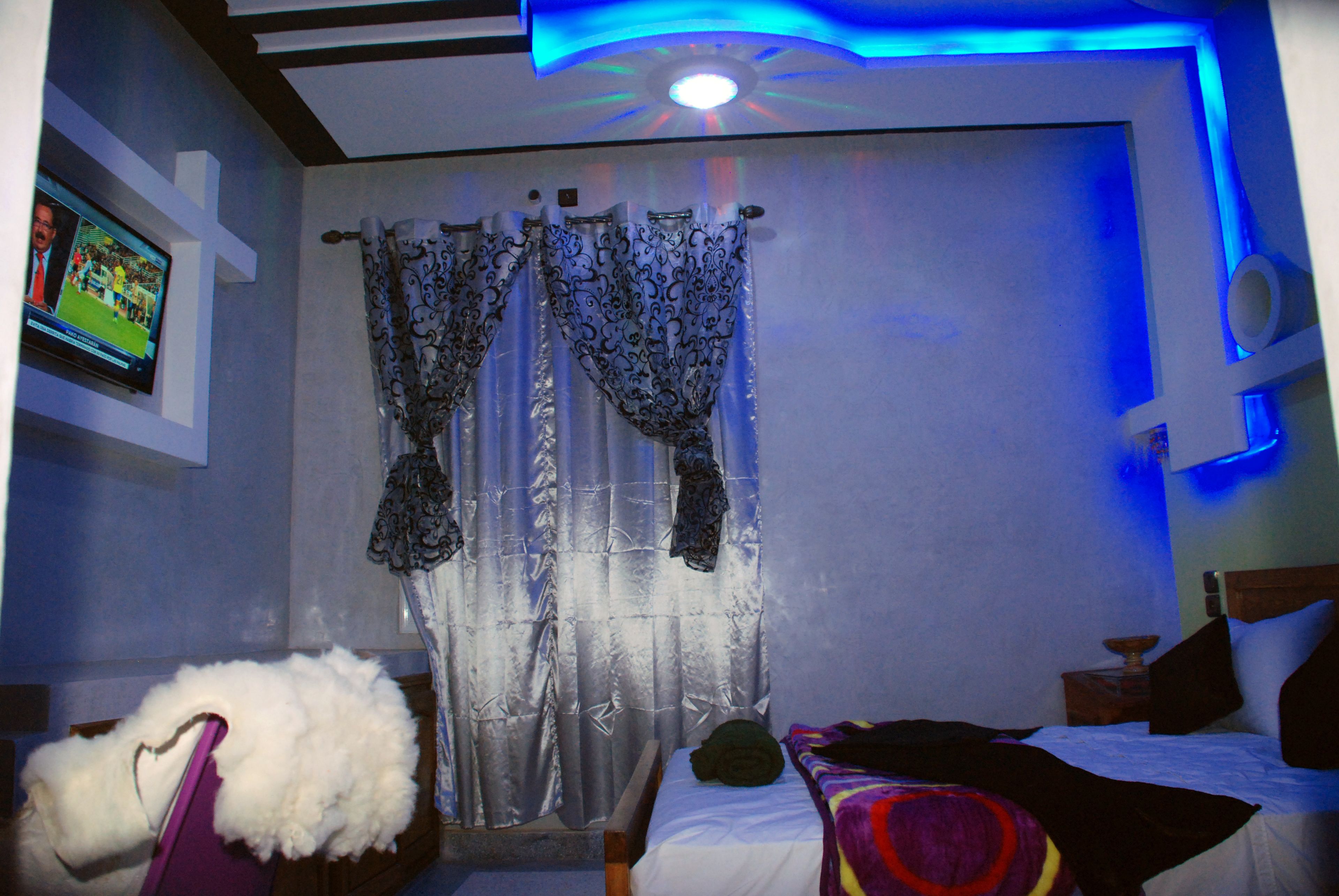 Quarto com uma cama, uma cadeira, uma televisão e uma janela com cortinas.