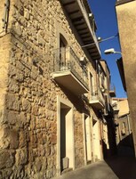 Uma rua estreita com edifícios de pedra, varandas e um céu azul claro.