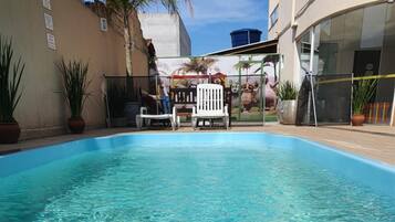 Piscina com água cristalina, cercada por plantas em vasos e um muro branco.