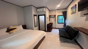 Quarto de hotel com uma cama grande, um sofá, uma TV e uma janela com cortinas.