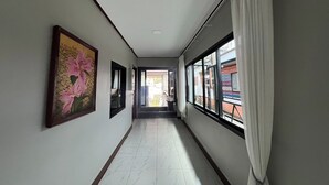 Um corredor com uma janela grande à direita, uma porta no final e um quadro pendurado à esquerda.