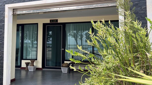 Entrada de um edifício moderno com porta preta, grandes janelas e uma pequena área externa com um banco e duas mesas decorativas.
