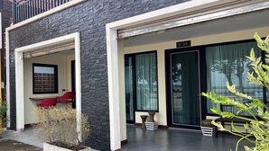 Um edifício moderno com fachada preta e detalhes brancos, com entrada por porta de vidro e uma pequena área externa com cadeiras vermelhas.