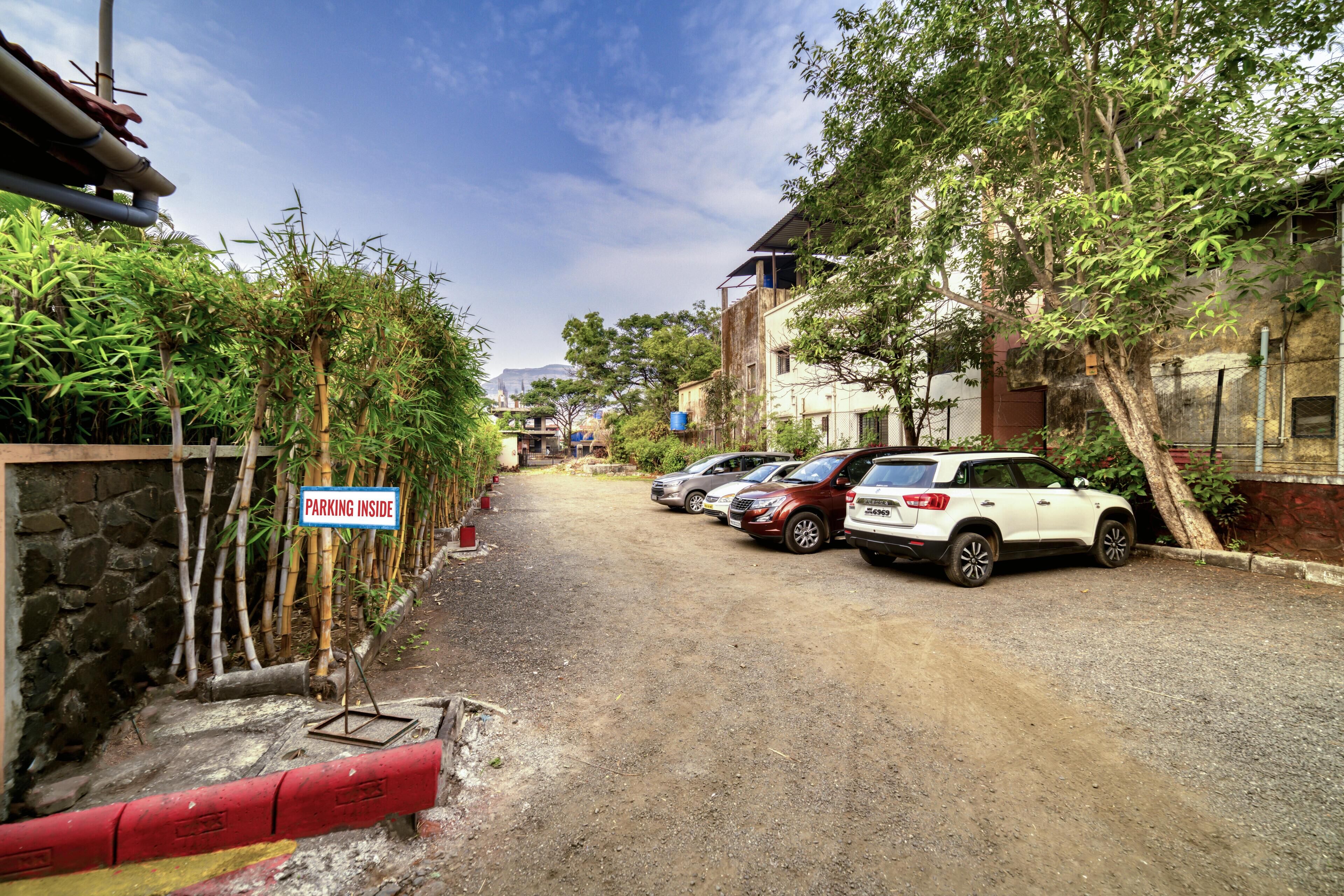 Uma área de estacionamento com carros estacionados ao longo de um caminho de terra, cercada por edifícios e vegetação.