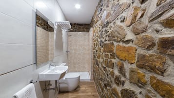 Casa de banho com parede de pedra, pia branca, sanita e zona de duche.