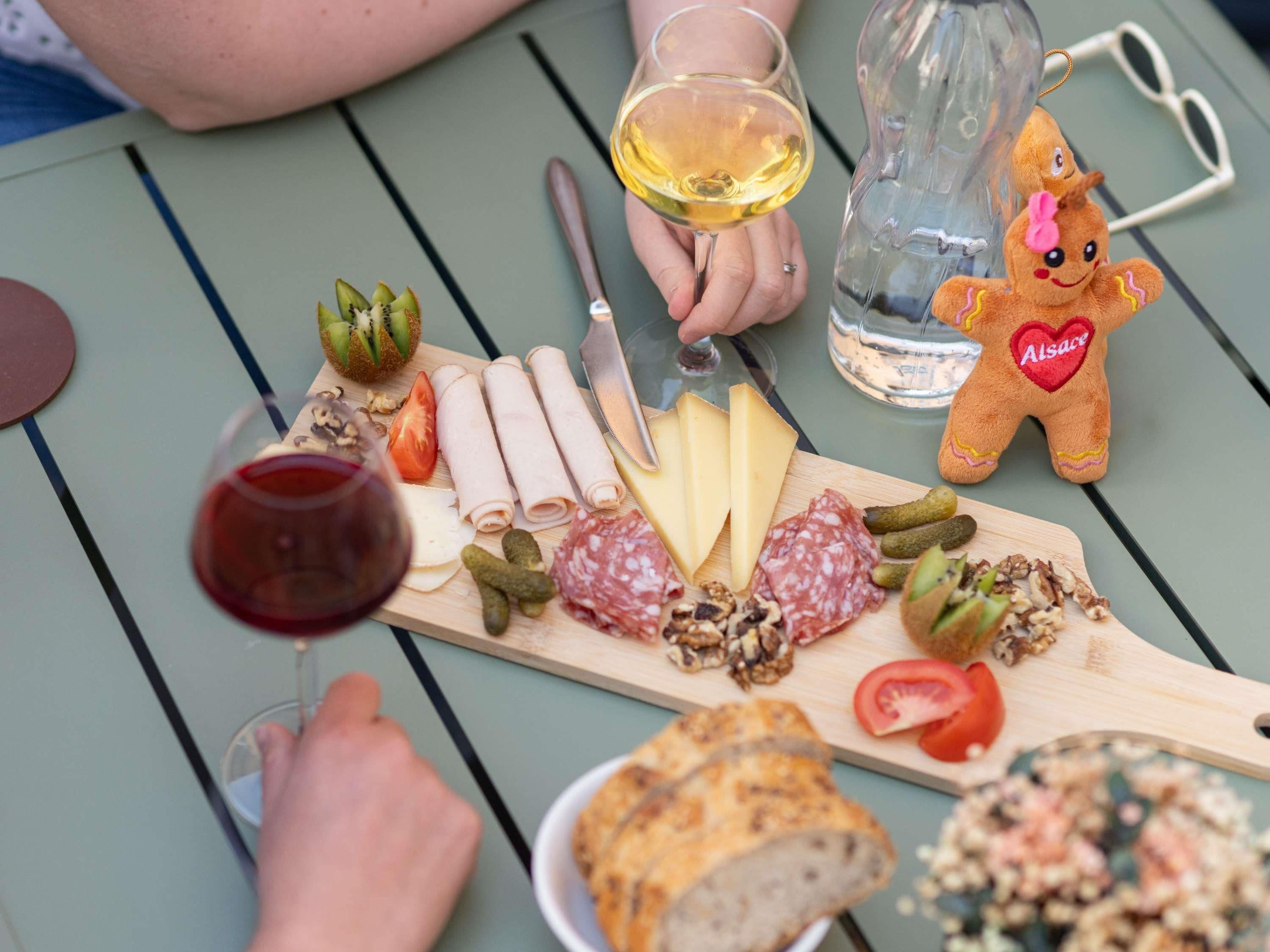 Tábua de madeira com diversos queijos, enchidos e legumes, acompanhada de copos de vinho e uma garrafa de água.