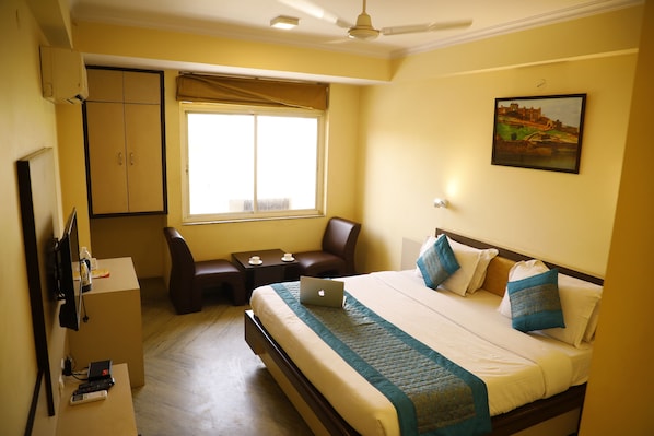 Quarto de hotel com uma cama, escrivaninha, cadeira, janela e um quadro na parede.