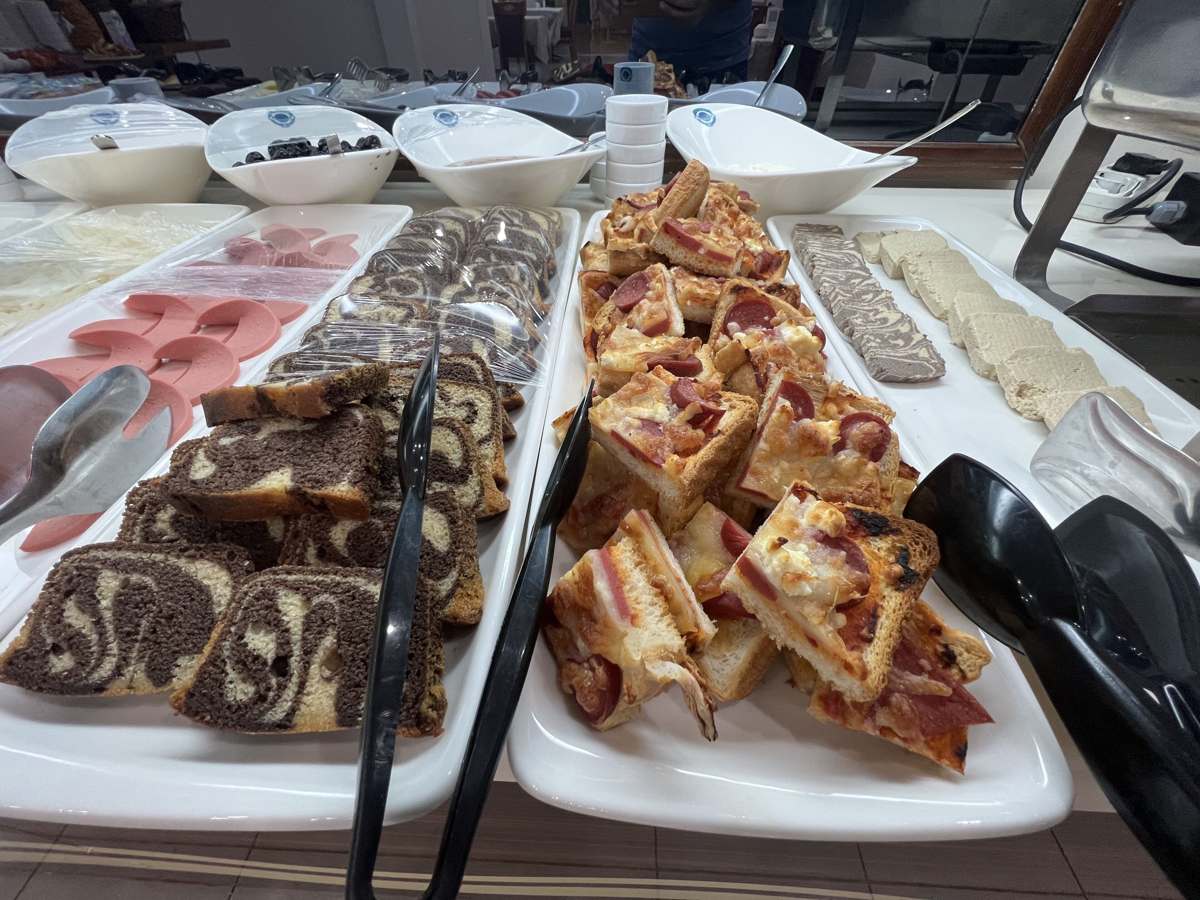 Mesa de buffet com diversos alimentos, incluindo pão, pastelaria e patês.