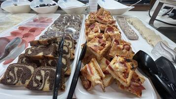 Mesa de buffet com diversos alimentos, incluindo pão, pastelaria e patês.