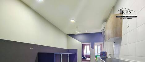Cozinha moderna com bancada escura, piso de azulejos brancos e vista para um quarto com cama e cortinas.