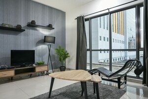 Sala de estar moderna com televisão de tela plana, móvel para eletrônicos de madeira, uma mesinha, um vaso de planta e uma janela grande com vista para a cidade.