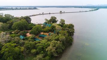 Vista aérea de uma propriedade à beira de um lago, com várias cabanas de telhado verde, rodeadas por vegetação densa.
